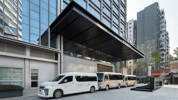 Um edifício moderno com fachada de vidro e entrada coberta. Três vans brancas estão estacionadas na frente.