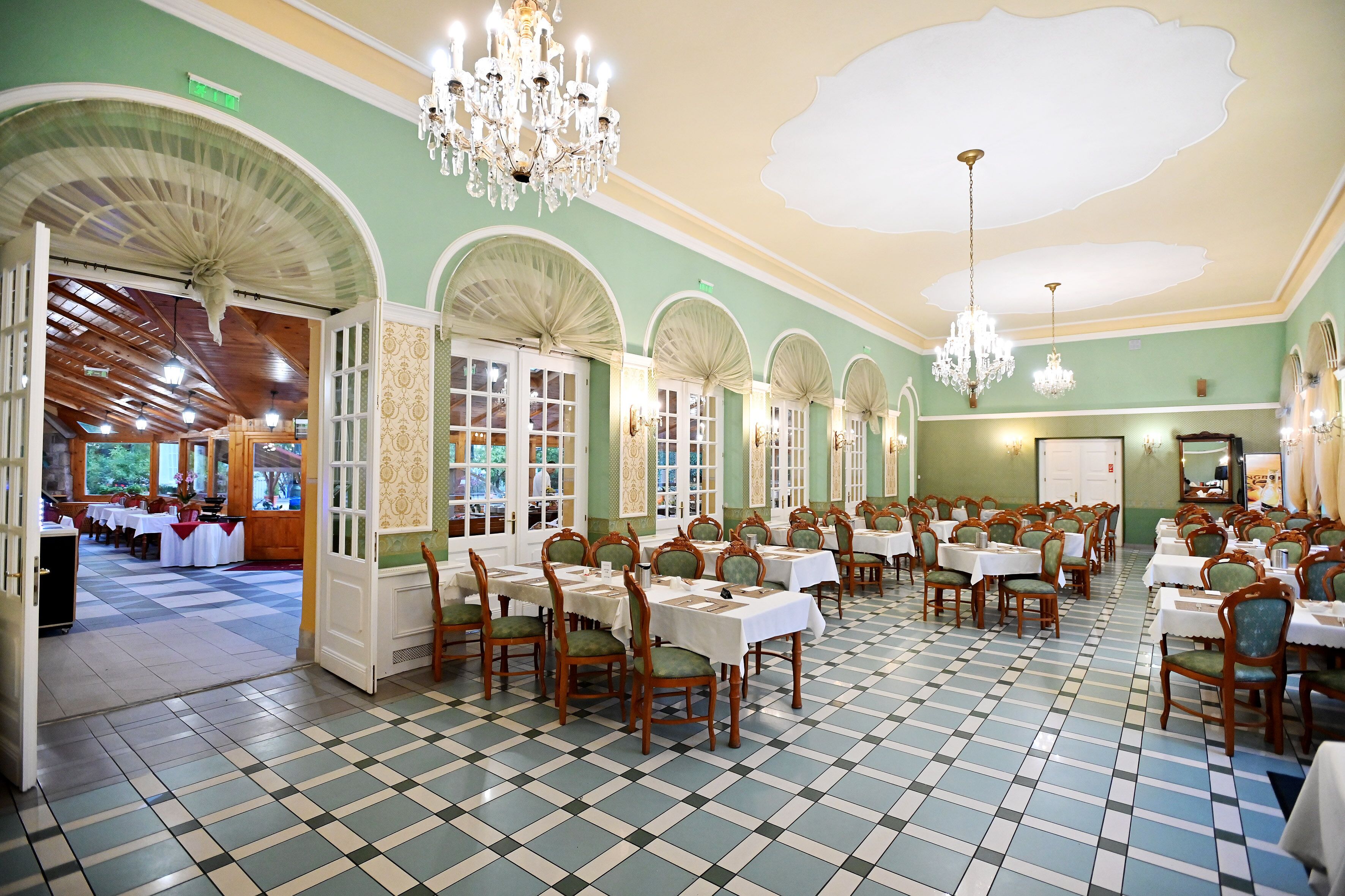 Uma sala de jantar com mesas, cadeiras, lustres e piso xadrez.