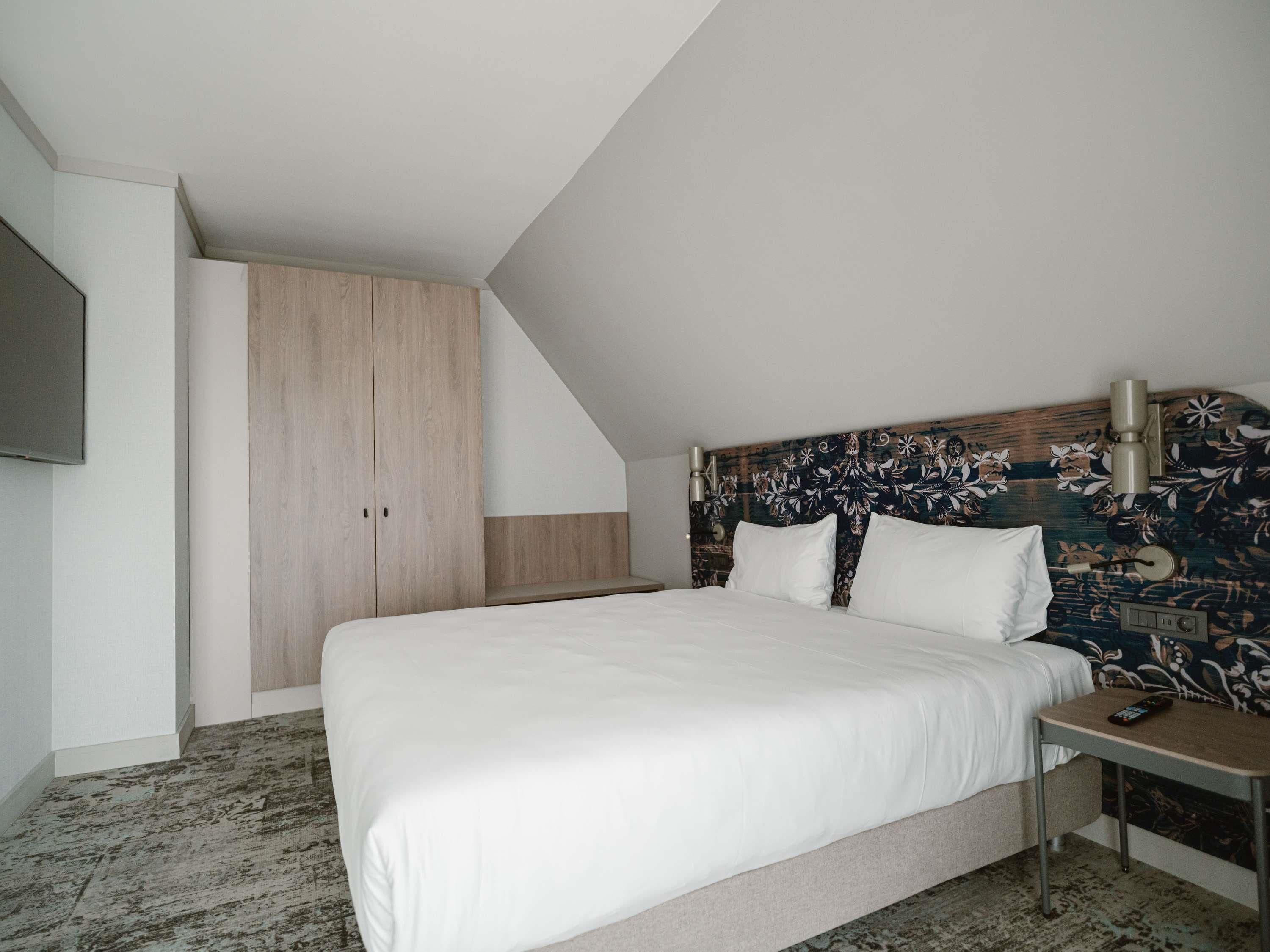 Quarto com cama, mesa de cabeceira, televisão e guarda-roupa.