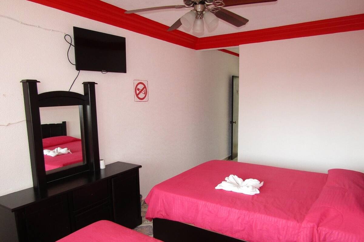 Quarto de hotel com duas camas, televisão, ventoinha no teto e placa de proibido fumar.