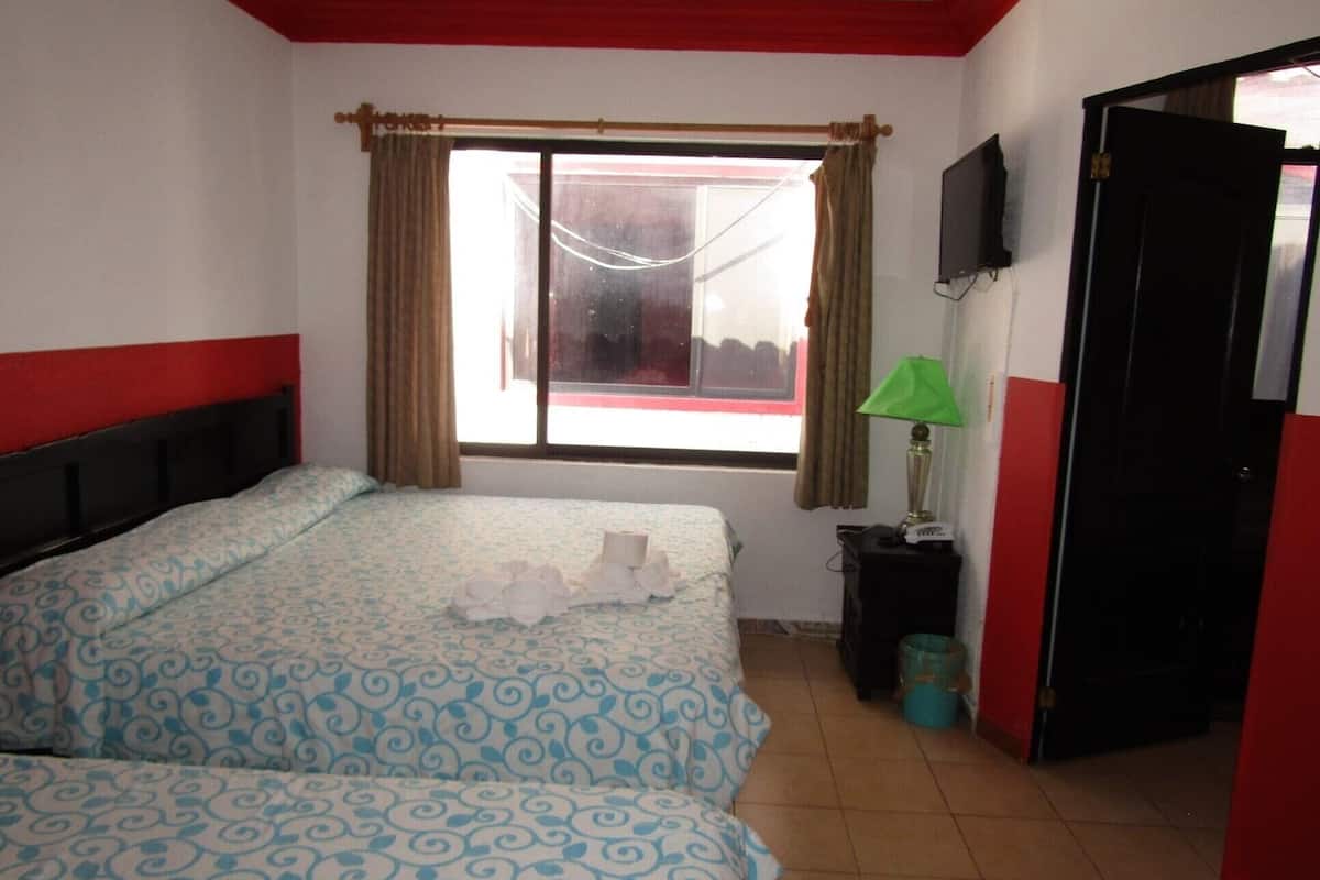 Quarto com duas camas, uma janela com cortinas, uma televisão e um abajur verde.