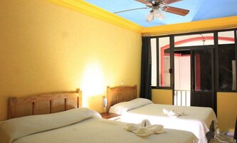 Quarto de hotel com duas camas, ventilador de teto e janela com vista para o exterior.