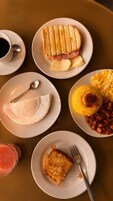 Uma mesa com diversos itens de pequeno-almoço, incluindo panquecas, ovos mexidos e uma fatia de bolo.