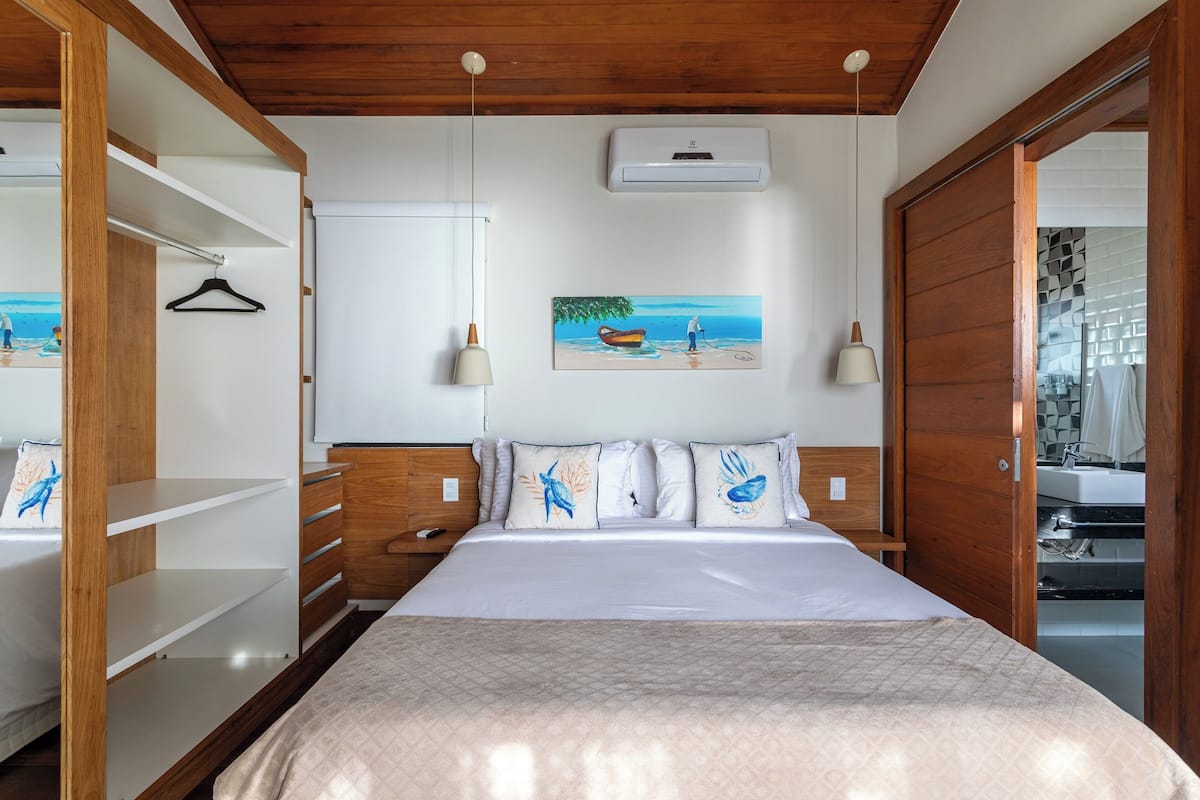 Quarto com cama, luminária pendente, pintura e guarda-roupa de madeira.