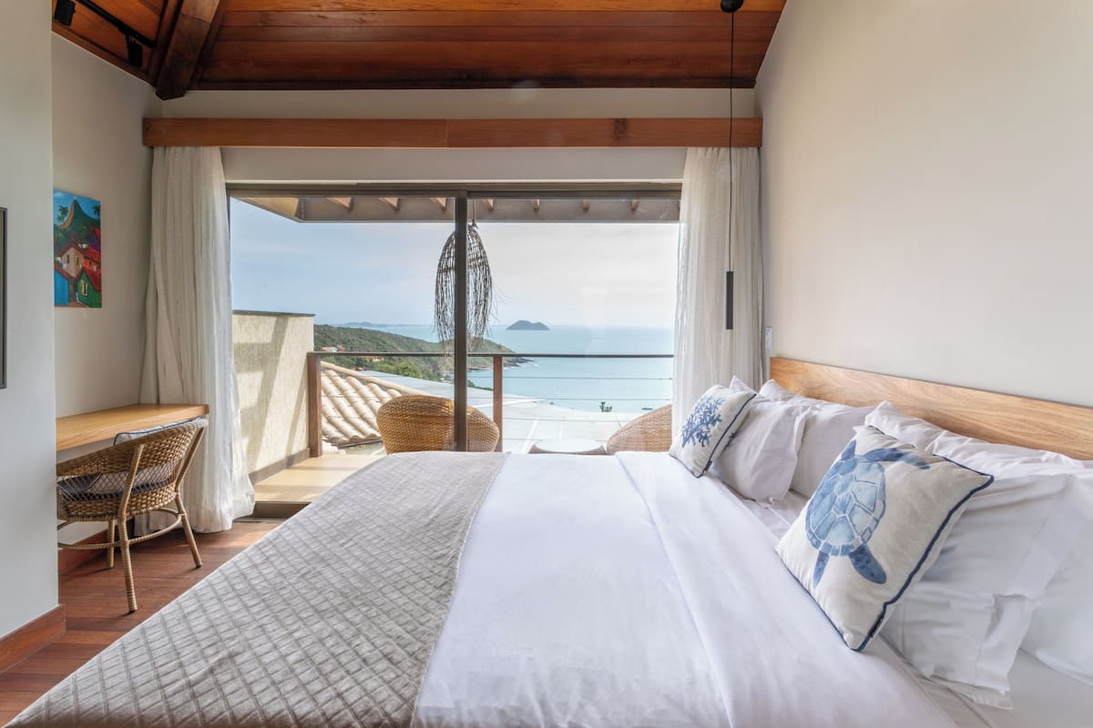 Quarto com uma cama grande, uma escrivaninha e vista para o mar.