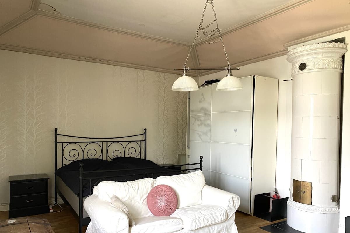 Quarto com cama, sofá branco, guarda-roupa e um pilar branco.