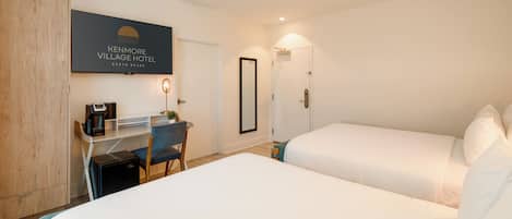 Quarto de hotel com duas camas, uma escrivaninha com computador, cafeteira e TV fixada na parede exibindo o nome do hotel.