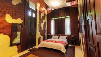 Quarto com parede de tijolos, porta de madeira e cama com colcha e almofadas brancas.