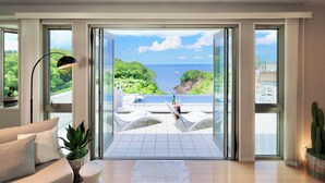 Sala de estar moderna com uma grande porta de vidro deslizante que dá para uma varanda com vista para o mar e vegetação.