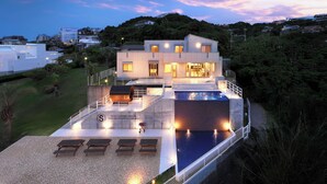 Uma casa moderna com piscina, área externa coberta e vista para as colinas ao redor.