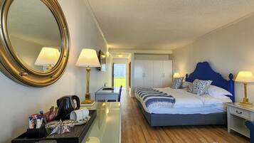Quarto de hotel com um espelho grande, cama com roupa de cama azul e branca, escrivaninha com cafeteira e produtos de higiene pessoal, e um guarda-roupa.