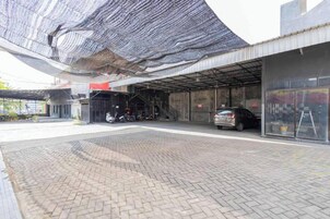 Uma área de estacionamento coberta com piso de tijolos, um carro e uma motocicleta.