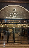 Entrada de hotel com uma grande porta em arco, portas de vidro e uma placa com o nome do hotel em vários idiomas.