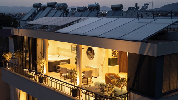 Um edifício moderno com telhado plano, painéis solares e varanda com plantas em vasos.