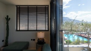 Quarto com cama, luminária, um cacto e vista para uma piscina e montanhas.