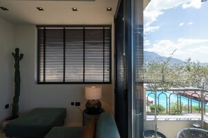 Quarto com cama, luminária, um cacto e vista para uma piscina e montanhas.
