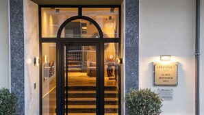 Entrada de hotel com porta de vidro, escadaria que leva ao interior e placa indicando 'EVRIPIDOU 7 KALAMATA MEDITERRANEAN SUITES'.