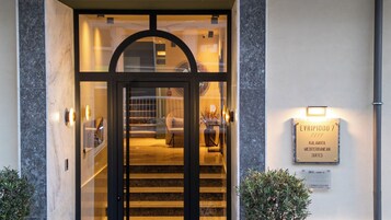 Entrada de hotel com porta de vidro, escadaria que leva ao interior e placa indicando 'EVRIPIDOU 7 KALAMATA MEDITERRANEAN SUITES'.
