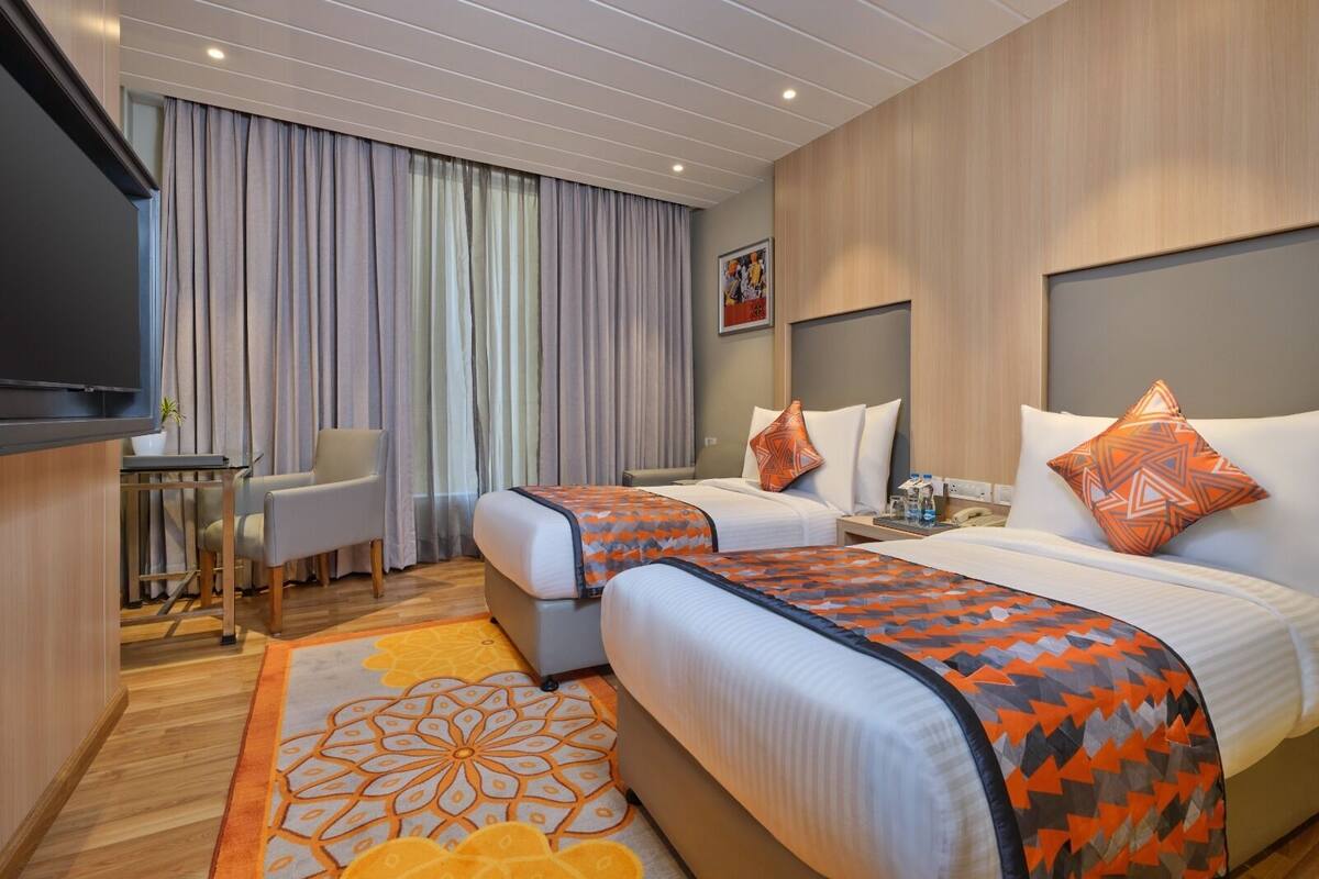 Quarto de hotel com duas camas, televisão, escrivaninha e uma cadeira.