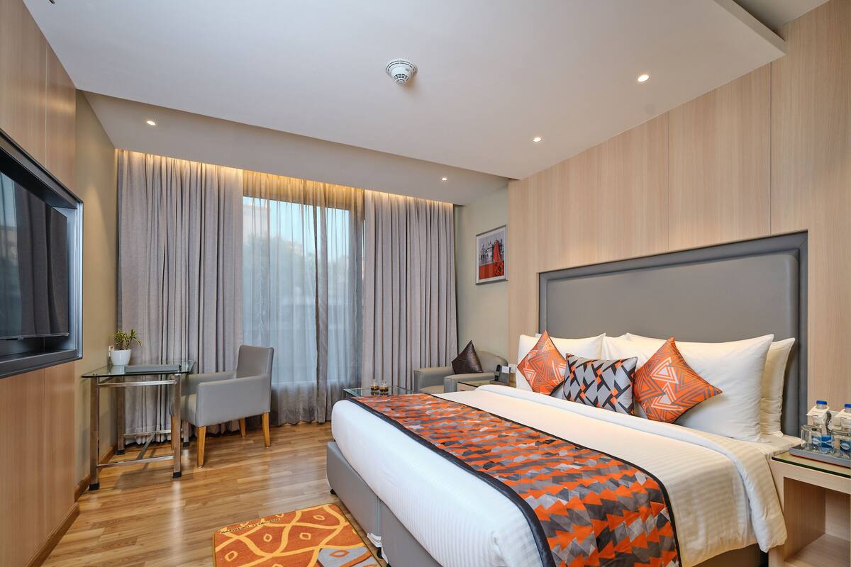 Quarto de hotel moderno com uma cama grande, uma escrivaninha, uma cadeira e uma televisão.