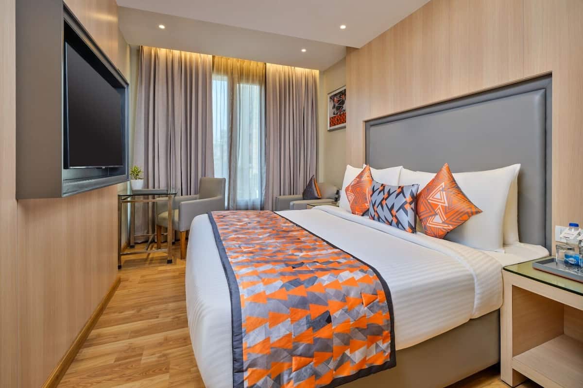 Quarto de hotel moderno com uma cama grande, televisão de tela plana, escrivaninha e uma cadeira.