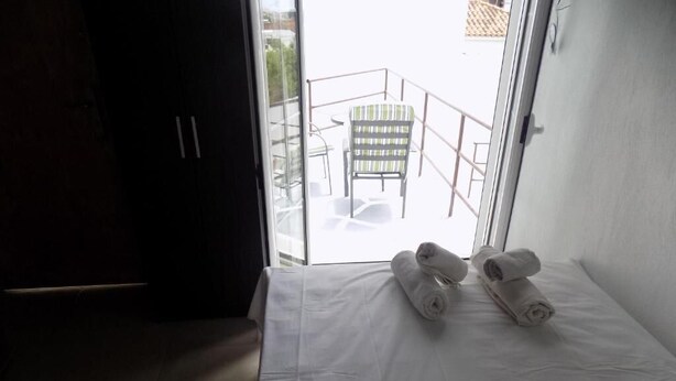 Quarto de hotel com cama, janela e vista para uma varanda externa com cadeira e mesa.