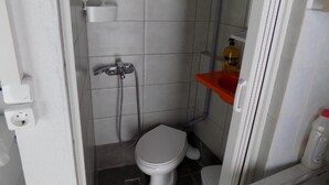Casa de banho pequena e compacta, com sanita branca, área de chuveiro e lavatório vermelho.