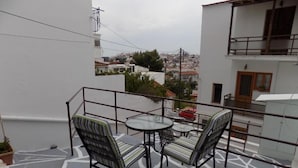 Uma varanda com mesa e cadeiras, vista da cidade e um edifício branco ao fundo.