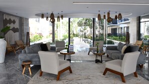 Uma área de estar moderna com sofás e mesas redondas, amplas janelas com vista para o verde e iluminação pendente.