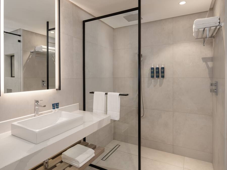 Uma casa de banho moderna com um espelho grande, lavatório branco e cabine de duche com vidro.
