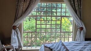 Quarto com cama, janela com cortinas e vista para o verde lá fora.