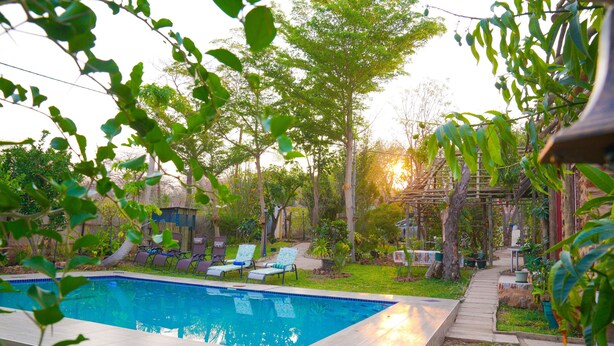 Piscina com cadeiras de descanso, rodeada por vegetação e árvores.