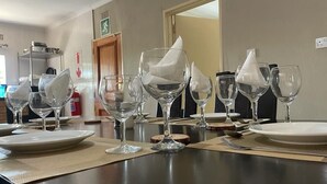 Mesa de jantar posta com taças de vinho e pratos, com um extintor de incêndio e placa de saída visíveis ao fundo.