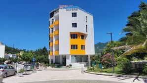 Um hotel com vários andares, varandas, área de estacionamento e um jardim ajardinado.