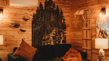 Interior acolhedor de uma cabana, com paredes de madeira, um mural de uma grande árvore, um sofá, uma mesa de centro e uma luminária.
