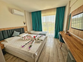 Quarto de hotel com duas camas, uma escrivaninha de madeira, uma televisão e uma varanda com cortinas.