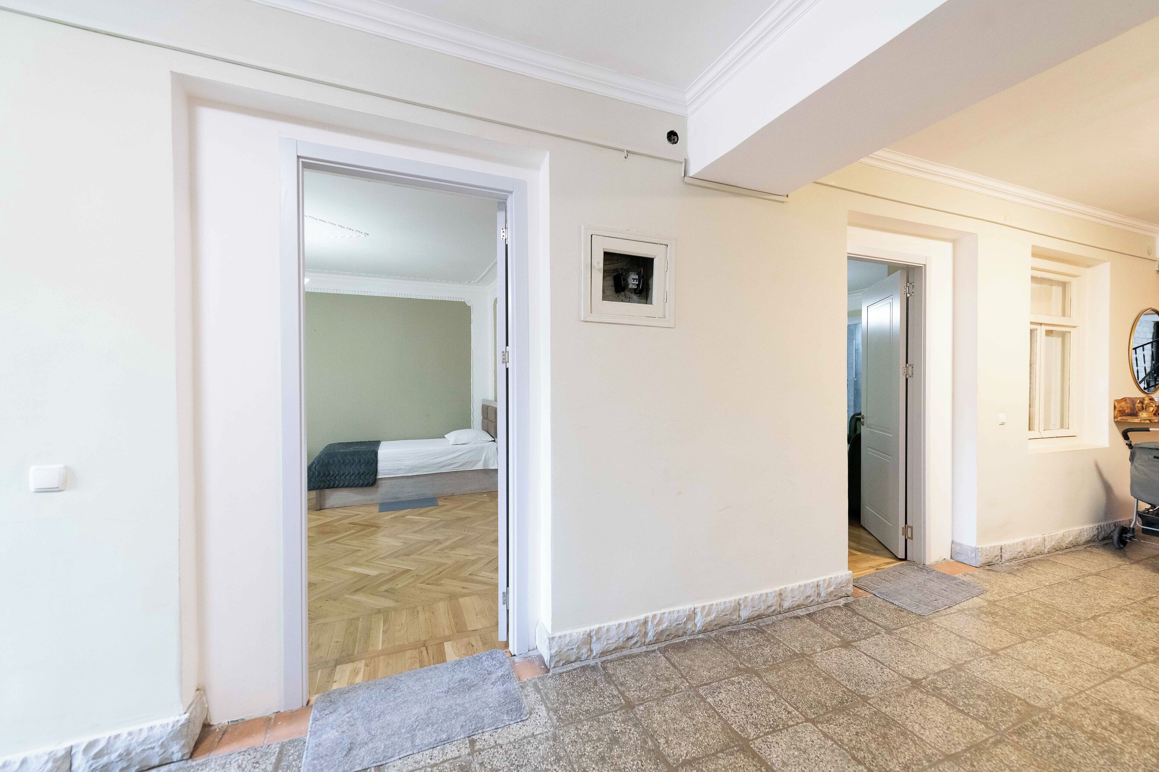 Um corredor com piso de madeira, uma porta que dá para um quarto e uma pequena janela.