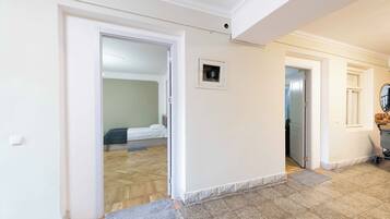 Um corredor com piso de madeira, uma porta que dá para um quarto e uma pequena janela.