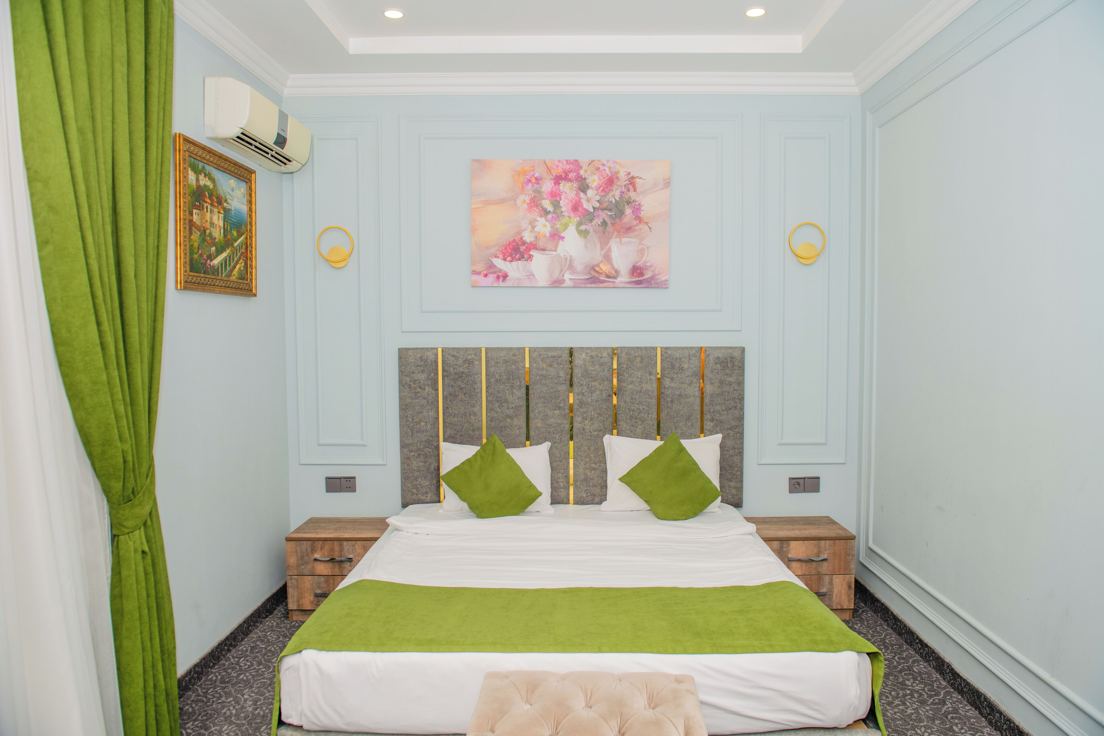 Quarto com cama, cortinas verdes, um quadro e uma mesinha de cabeceira de madeira.