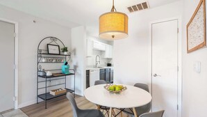 Uma cozinha moderna com armários brancos, um lustre pendurado e uma área de jantar com mesa e cadeiras redondas.