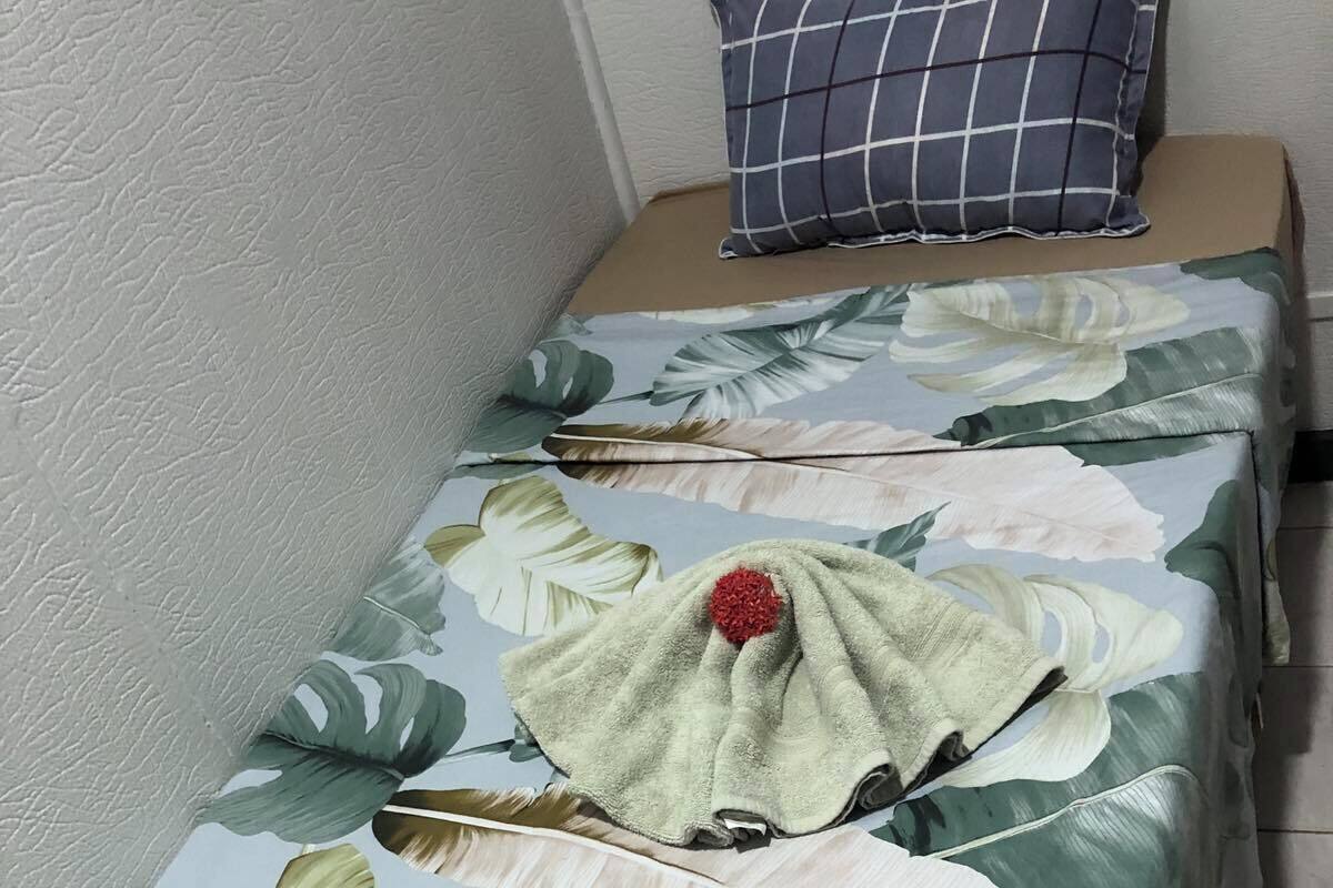 Uma cama de solteiro com um cobreleito floral, um travesseiro pequeno e um objeto decorativo vermelho sobre a cama.