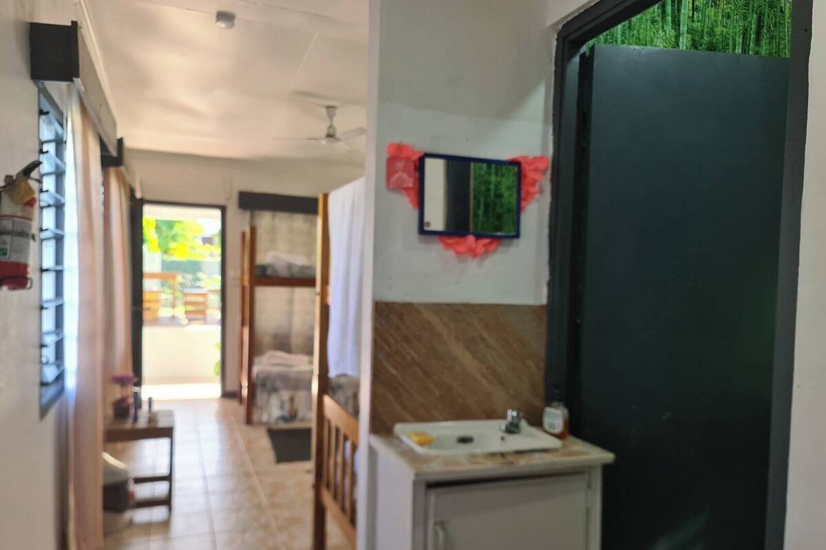 Um corredor com piso de azulejos, uma cama beliche ao fundo, uma pia com espelho e uma porta com tela verde.