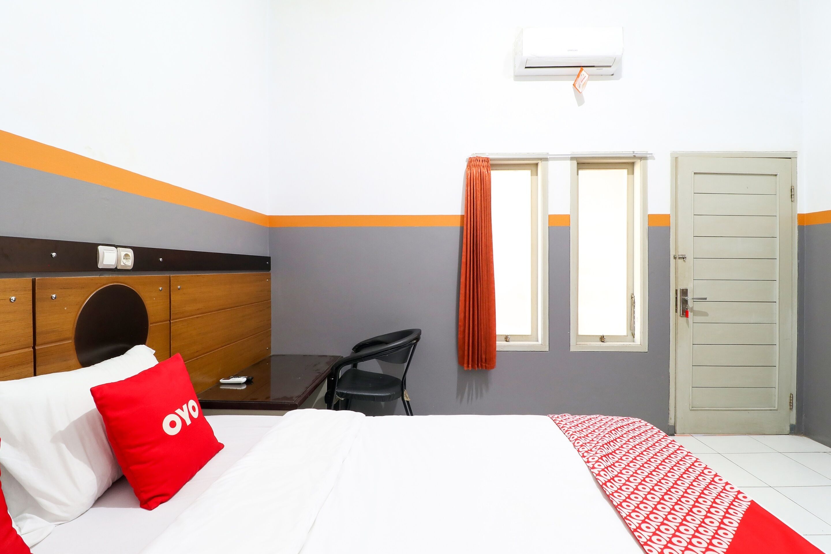 Quarto de hotel com cama, escrivaninha, cadeira, guarda-roupa e porta.