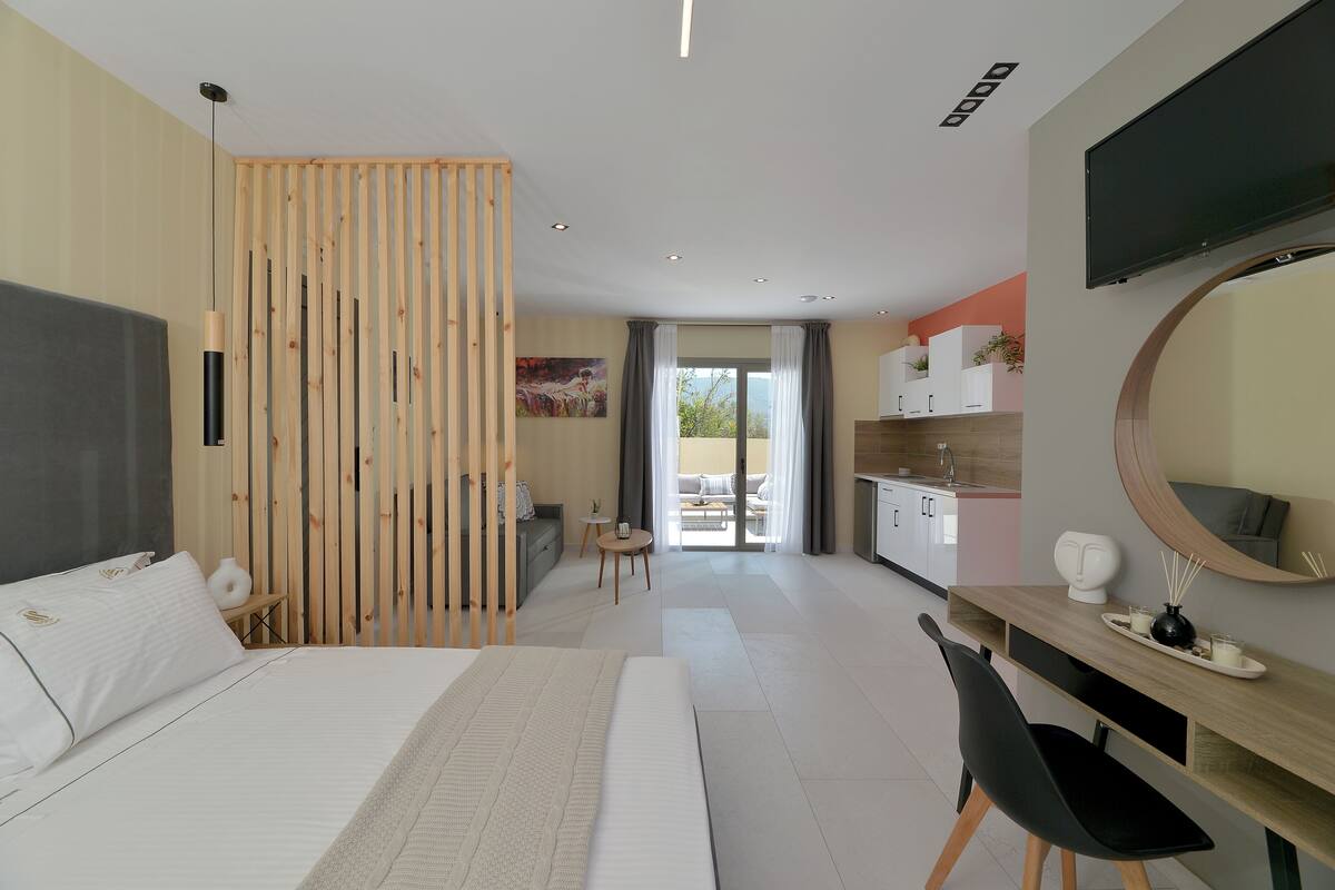Quarto de hotel moderno com uma cama grande, uma escrivaninha com cadeira, uma TV na parede e vista para a área externa.