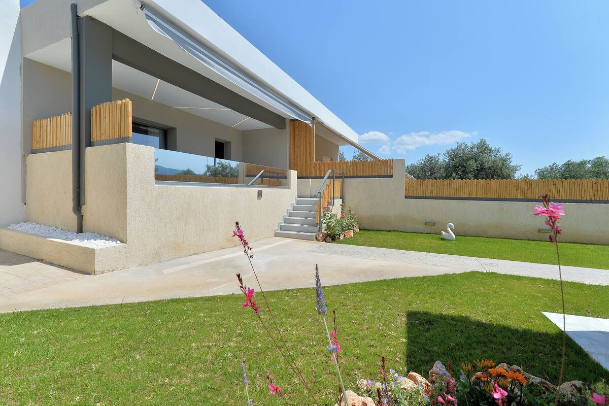 Uma casa moderna com varanda coberta, escada aparente e gramado bem cuidado com flores.