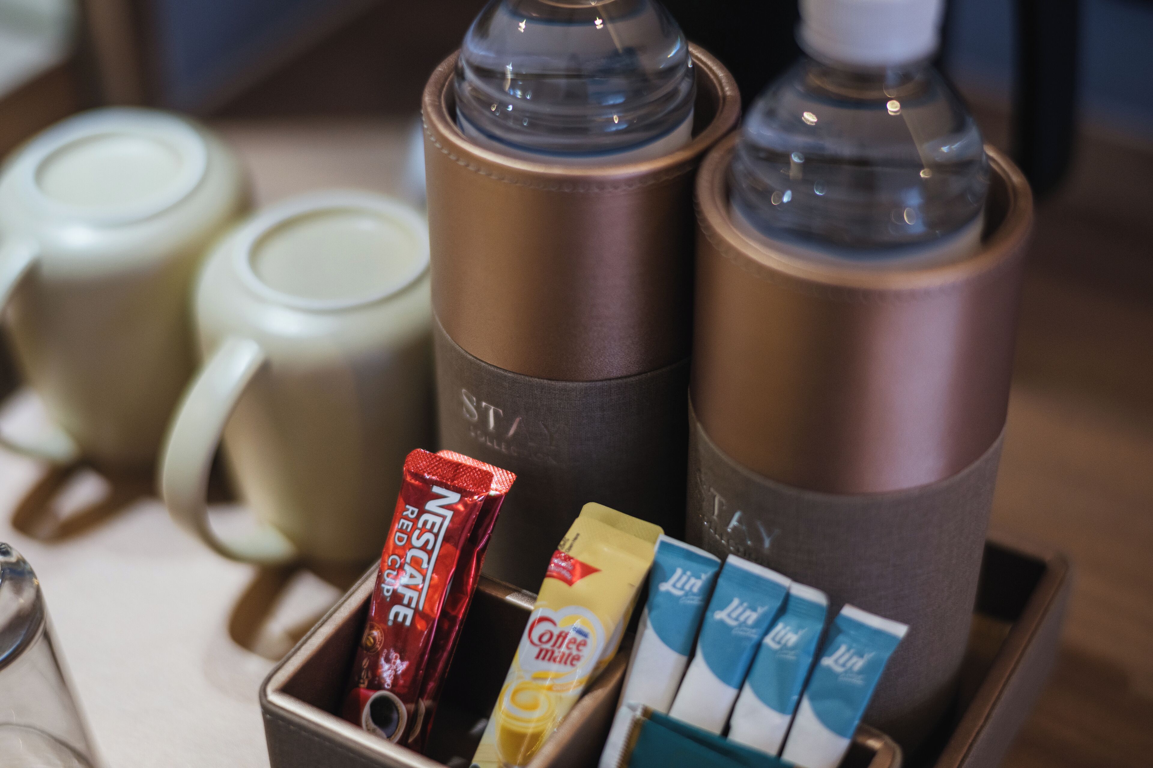 Um espaço para café com dois dosadores de aço inoxidável, uma caneca de café e embalagens de Nescafe Red Cup e Coffee Mate.