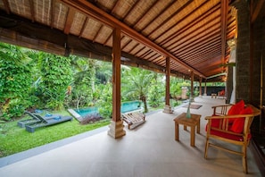 Uma área externa coberta com piscina, espreguiçadeiras e um banco de madeira.