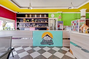 Uma área de recepção com balcão de check-in, um relógio e prateleiras com diversos objetos.