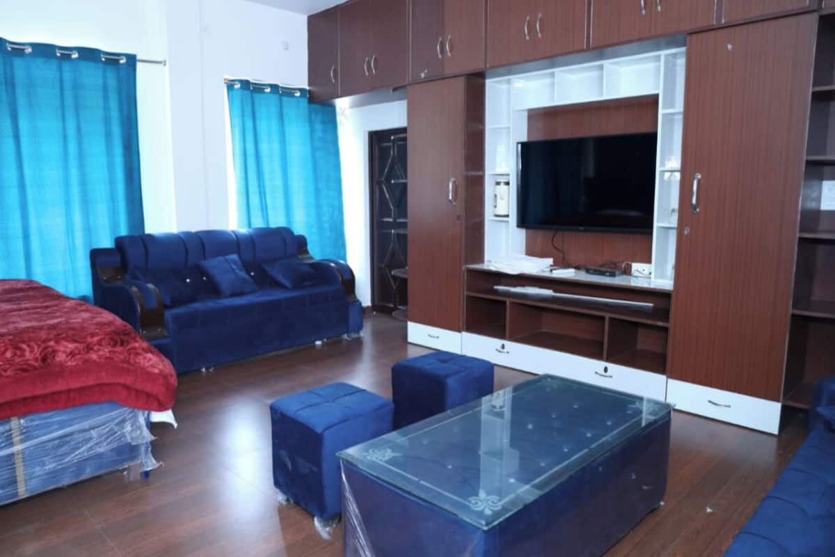 Espaço compacto com sofá, banquinho, mesa de centro de vidro e TV fixada em um móvel.