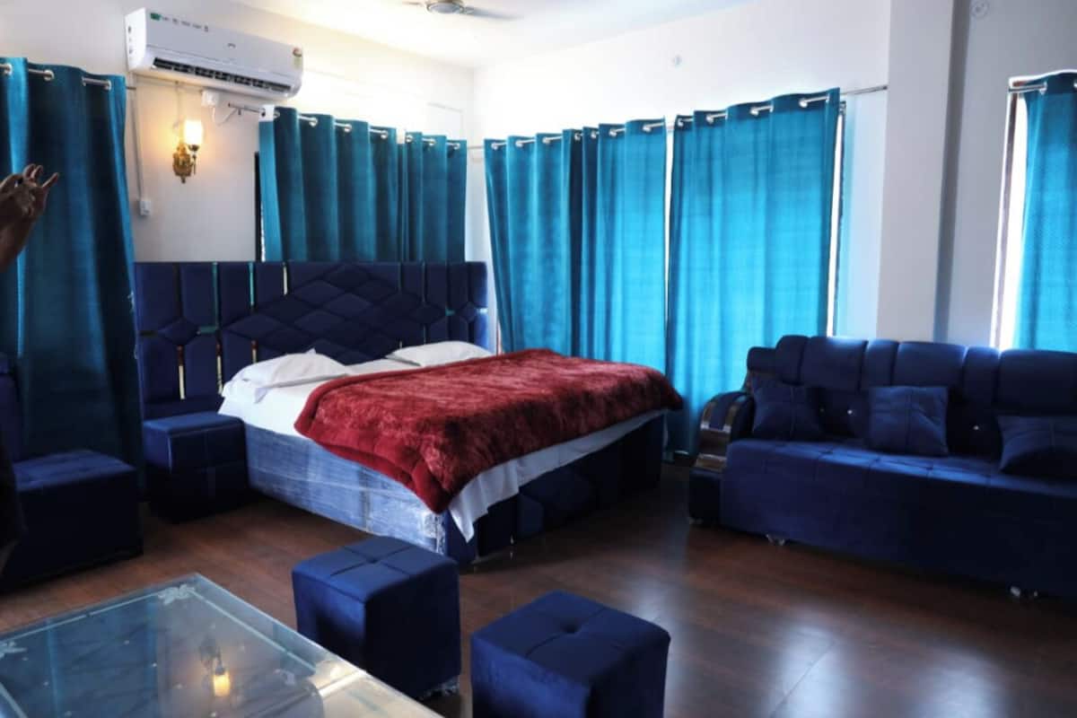 Quarto de hotel com cama, sofá, mesa de centro de vidro e ar condicionado fixado na parede.